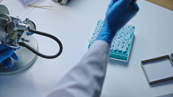 Male scientist examining liquid chemical substance under microscope lab ...