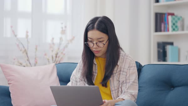 Relaxed Asian female programmer typing on laptop on couch, distance ...