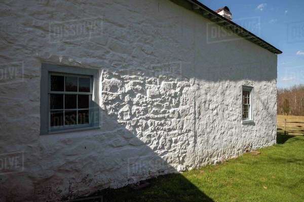 Evening shadows cross the side of a whitewashed stone colonial American ...