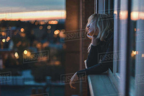 Portrait of a Caucasian woman leaning on the window at blue hour ...