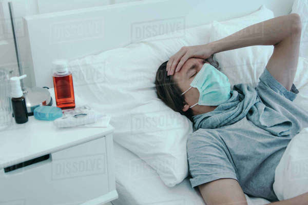 Sick man in bed holding his aching head because of fever. - Royalty ...