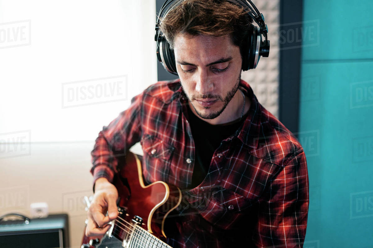 Young musician playing a guitar while working on songs during a ...