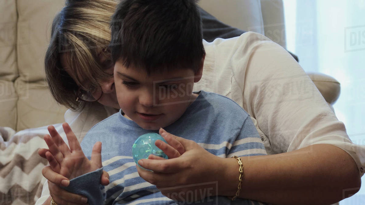 Child with disabilities on his mother's lap, playing with a rubber ball ...
