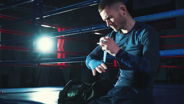 Bearded man in sportswear sitting on boxing ring and wrapping bandage ...
