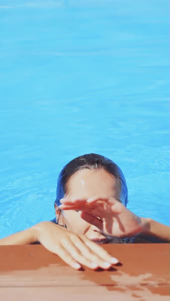 Vertical Screen: Woman in striped swimsuit emerges from pool water ...