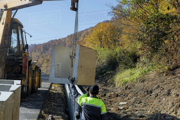 Concrete drain reconstruction workers installing precast square U-shape ...