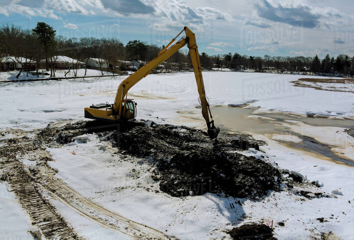 Cleaning the bottom of the lake with a excavators dredge on winter snow ...