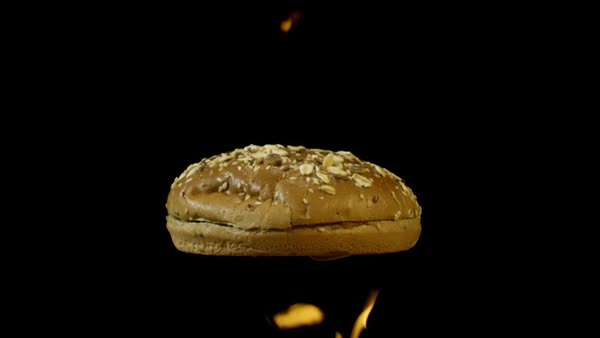 Close up of rotating burger bun in fire isolated on black background ...