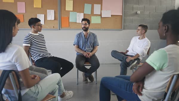 Teenager students talking and listening to friendly young male teacher ...