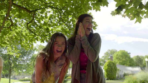 Two girls laugh hysterically, a friend comes over and hugs one girl ...