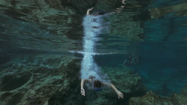 A woman jumps off a cliff into the ocean and swims underwater. Girl ...