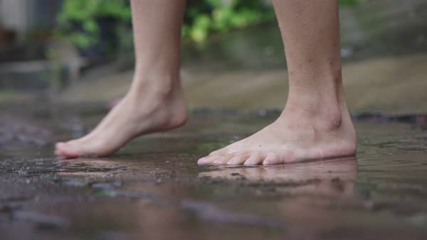 Close up of barefoot woman slowly stomping in water puddles on a paving ...