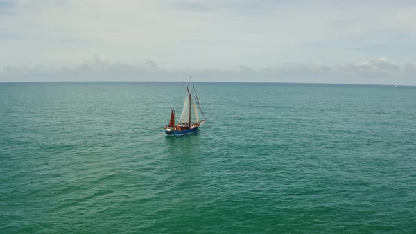 The sailing ship moves away from the land with sheer cliffs along the ...