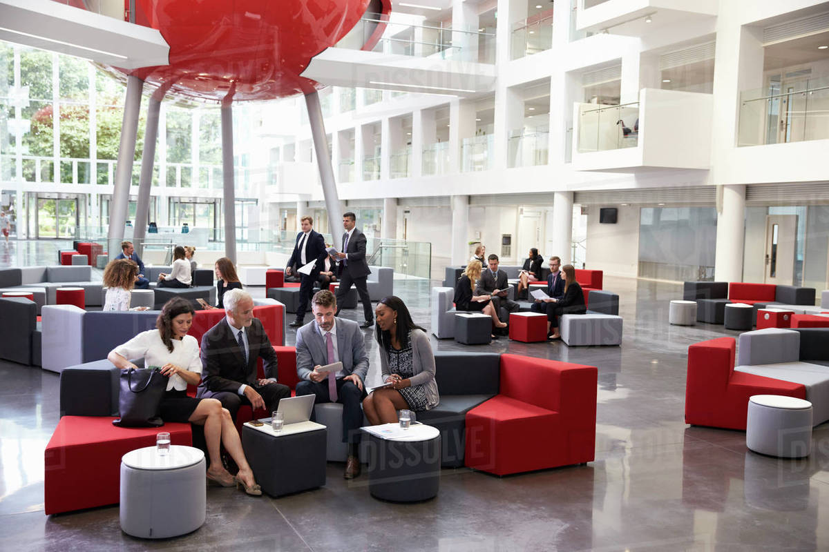 Businesspeople meeting in busy lobby of modern office - Royalty-free ...