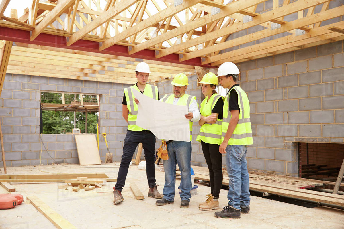 Builder on building site looking at plans with apprentices - Royalty ...