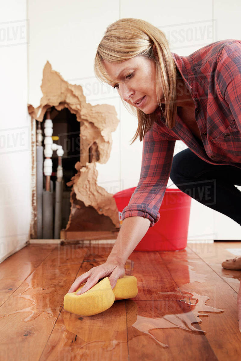 Woman mopping up water from a burst pipe with sponge, vertical ...