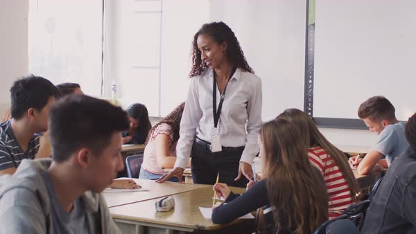 Female High School Teacher Talking To Student Sitting At Desks During ...