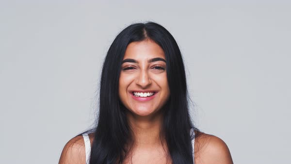 Young woman smiling and laughing into camera against white studio ...