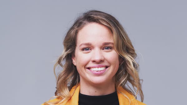 Close up of young woman smiling and laughing into camera against white ...