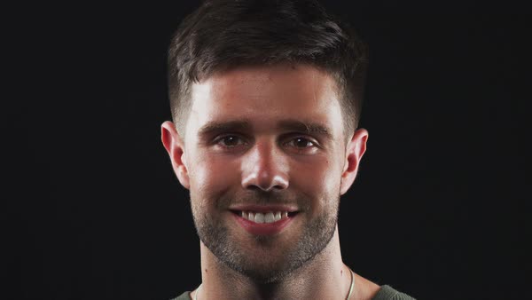 Close up of young man smiling and laughing into camera against black ...