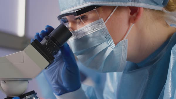 Female Lab Worker Wearing PPE Analysing Samples With Microscope Holding ...
