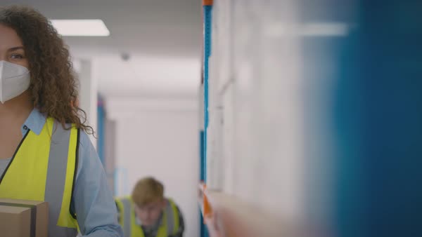 Camera tracks past warehouse shelves to show female worker in ...
