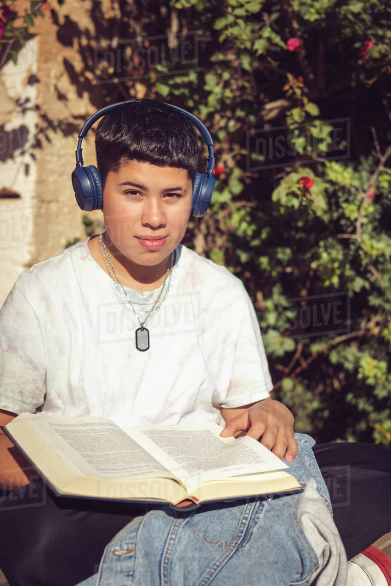 young student reading and listening to music sitting in the garden at ...