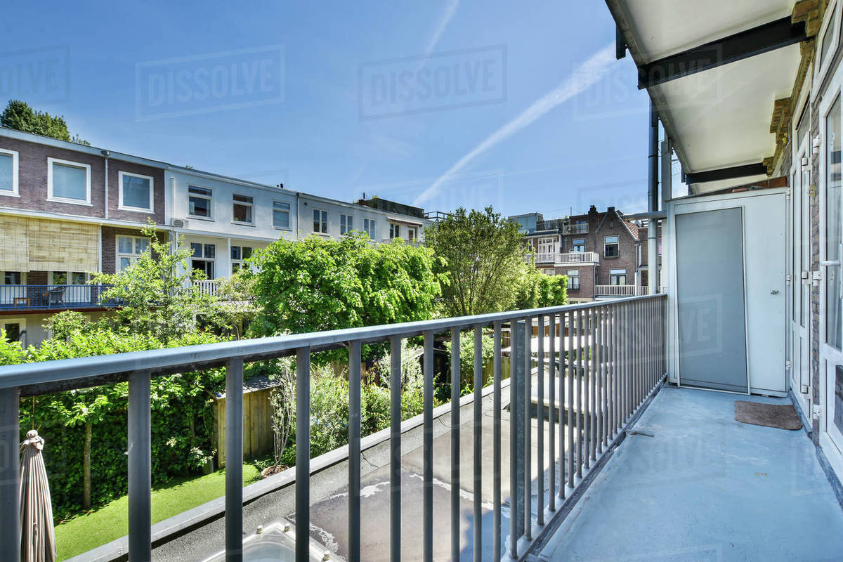 Balcony of modern flat with metal railing located against green trees ...