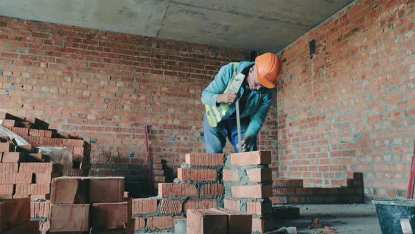 A builder on a construction site puts bricks in the house. Builder ...
