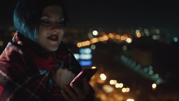 Woman uses a mobile phone at night and emotionally smiles and reacts to ...
