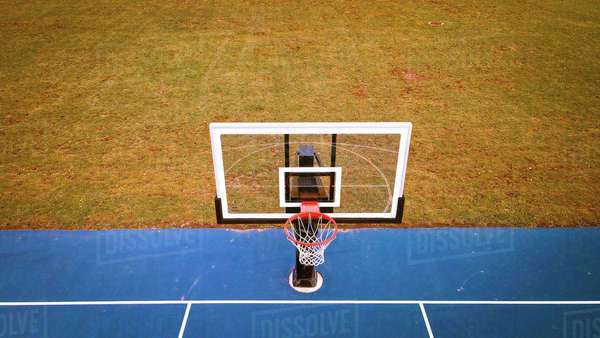 Clear basketball hoop with blue color at its base and yellow grass in ...