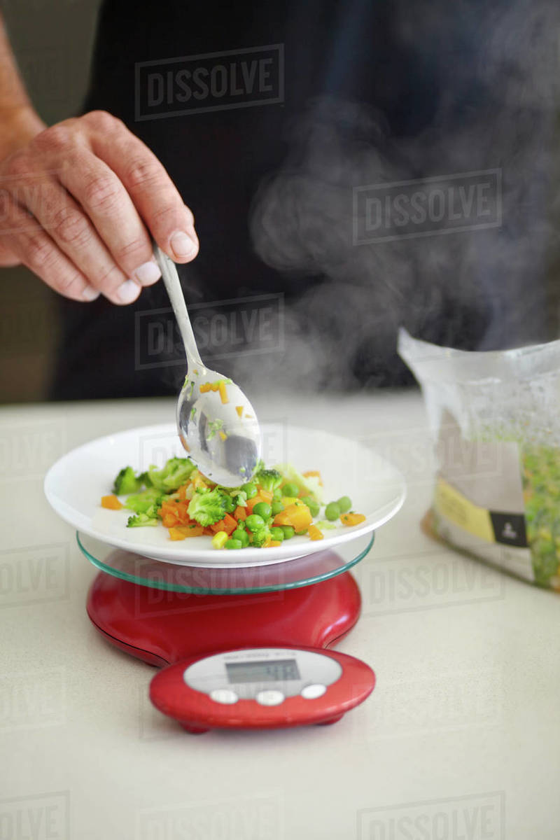 Scale, food and man with vegetables in kitchen to measure portion for ...