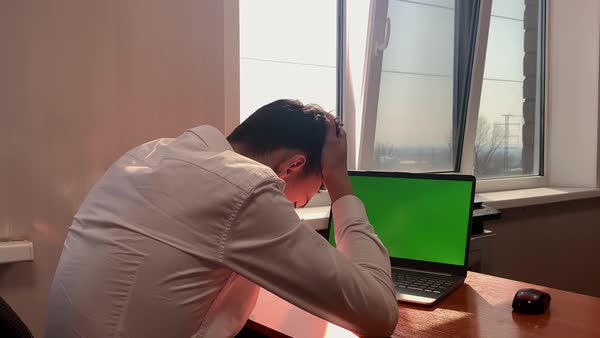 A young man sitting at a computer with a green screen in the office ...