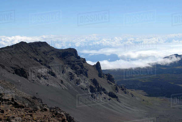 Basalt volcano cliffs curving into valley against cloud tops and sky in ...
