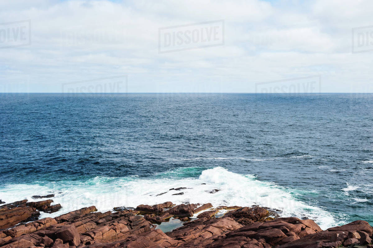 Churning water and waves splashing on rocky red coastline against ocean ...