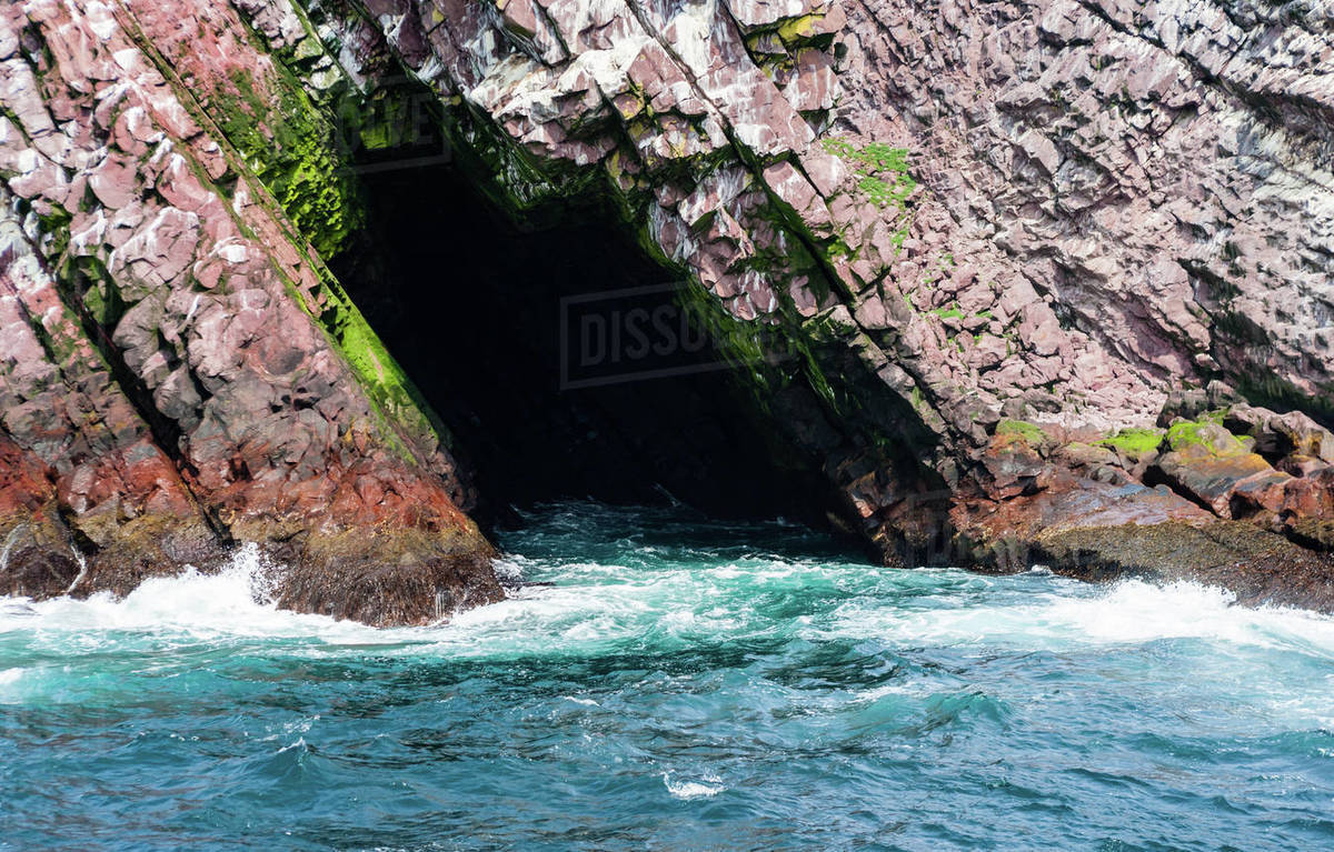 Churning water and waves splashing into diagonal cave in steep rocky ...
