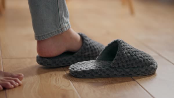 The girl slips her feet into a cozy pair of indoor slippers. As she ...