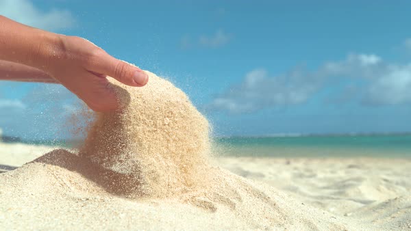 Particles of sand falling out of woman's grasp on a sunny exotic beach ...
