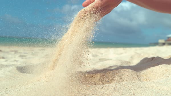 Countless grains of white sand fly out of woman's hands across exotic ...