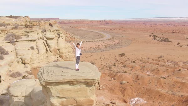 AERIAL: Happy female climber stands atop a boulder with her arms raised ...