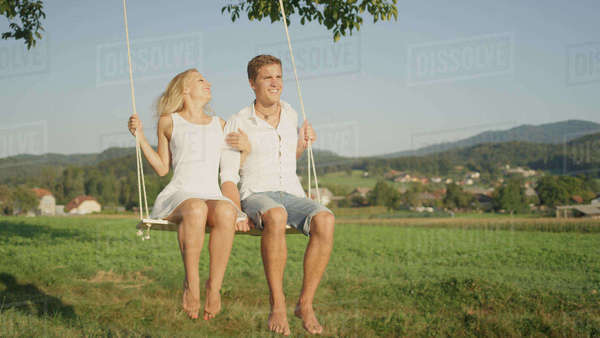 Charming young adults swinging on romantic swing on sunny afternoon ...