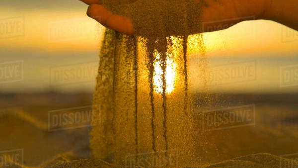 CLOSE UP: Small particles of dry sand fall between gentle unknown ...