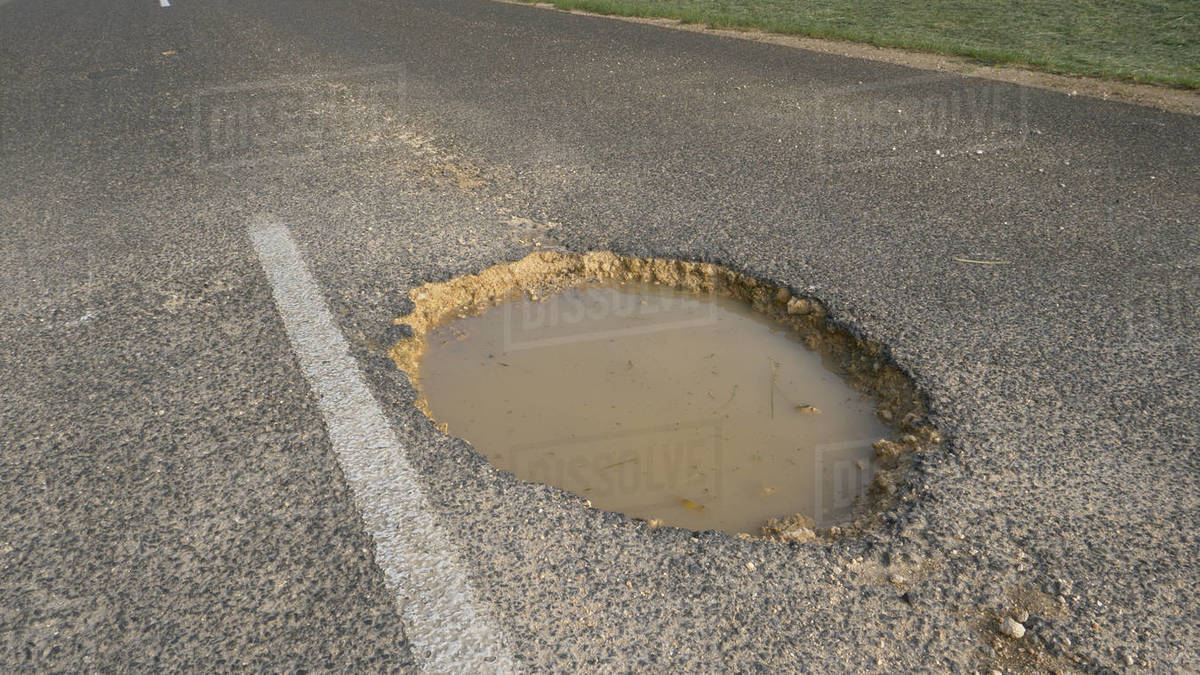 CLOSE UP: Large pothole in the middle of the road is filled with murky ...