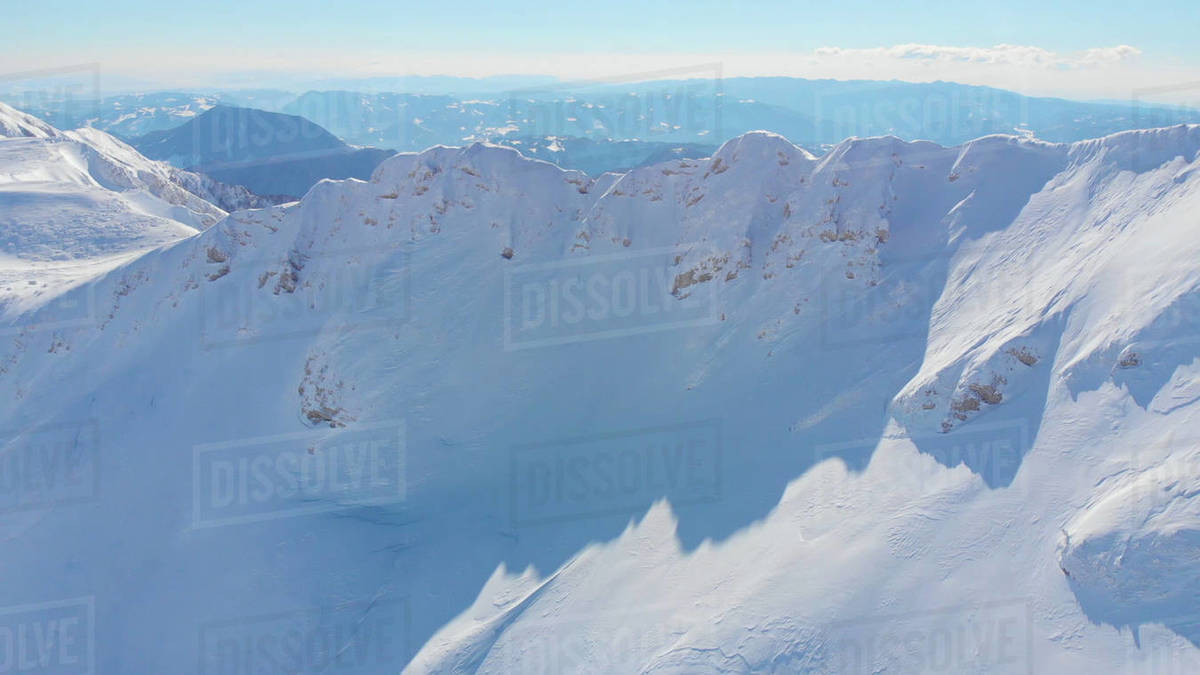 AERIAL: Flying towards the high summit of a snow covered mountain in ...
