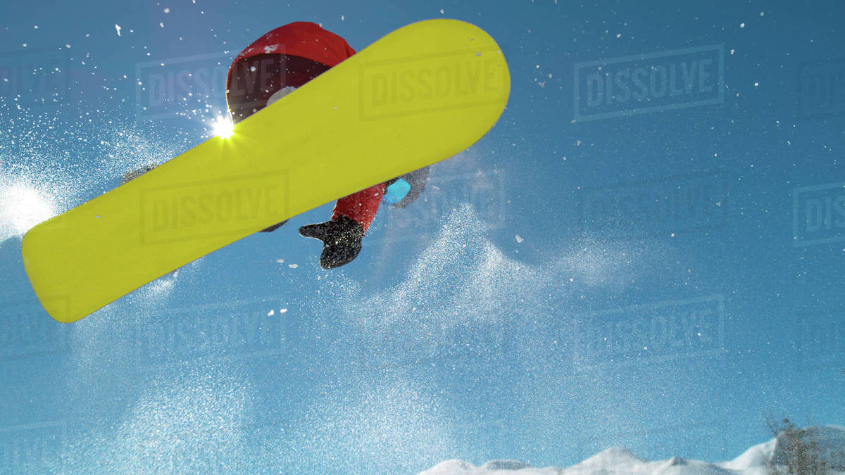 LENS FLARE, CLOSE UP: Young professional snowboarder jumps off kicker ...