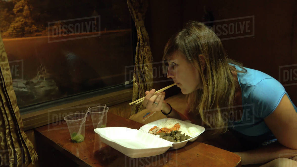 CLOSE UP: Young Caucasian woman eating dinner while travelling by night ...