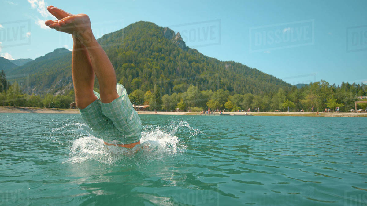 CLOSE UP: Playful male tourist jumps into the refreshingly cold lake on ...