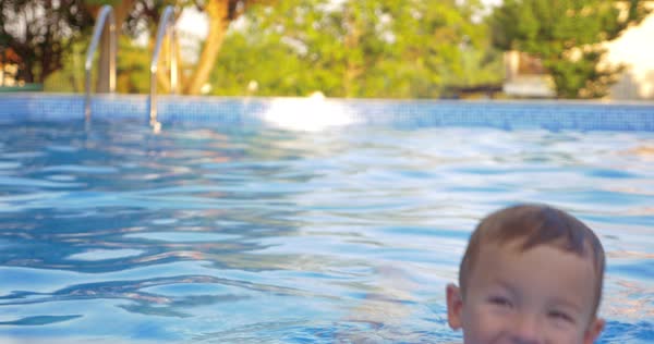 Little boy swimming alone in the outdoor pool. Funny kid enjoying ...