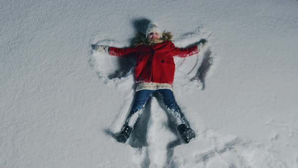 Top down footage of the happy cute little girl falling into snow, lying ...