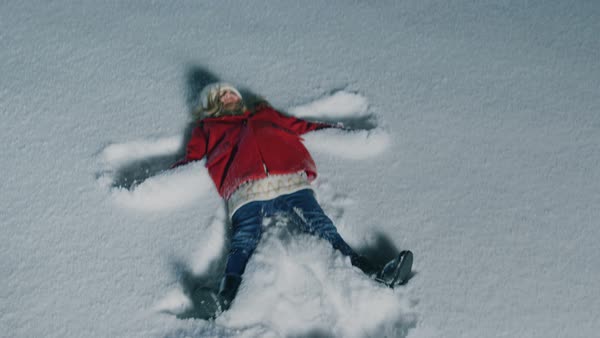 Top down footage of the happy cute little girl falling into snow, lying ...